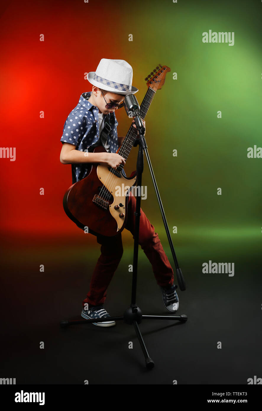 Little boy playing guitar and singing with microphone on a bright ...