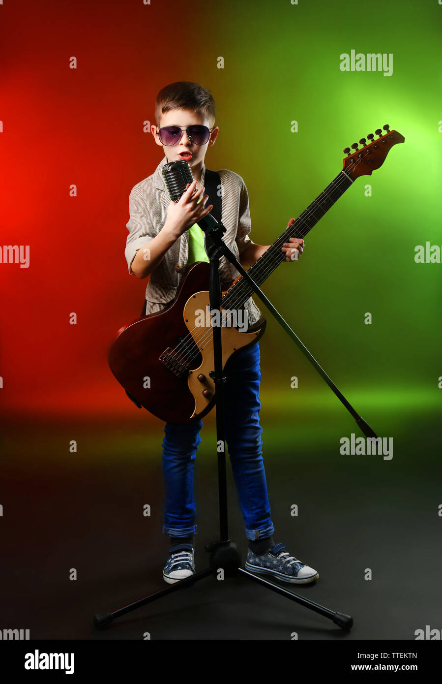 Little boy playing guitar and singing with microphone on a bright ...