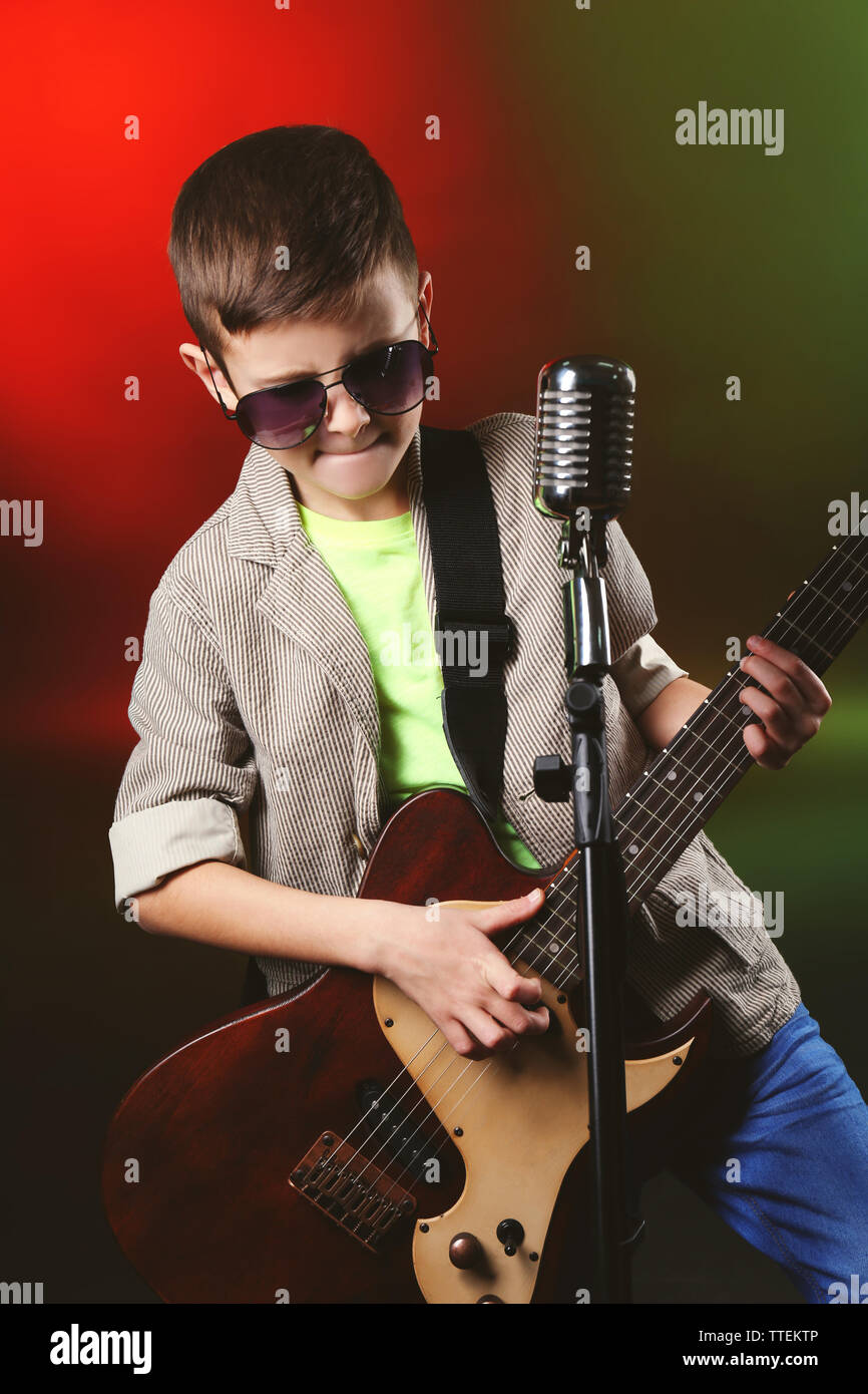 Little boy playing guitar and singing with microphone on a bright ...