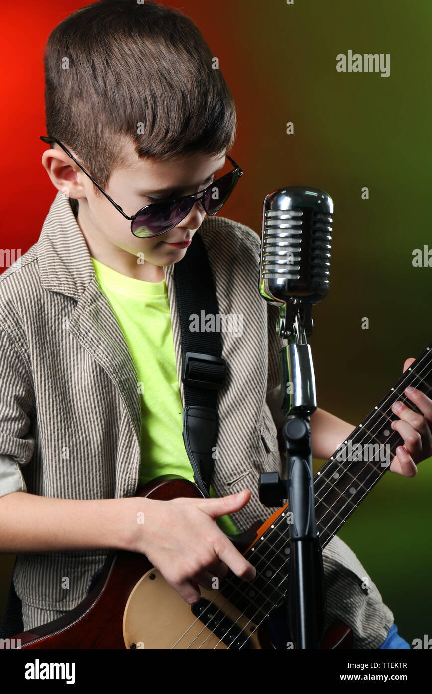 Little boy playing guitar and singing with microphone on a bright ...