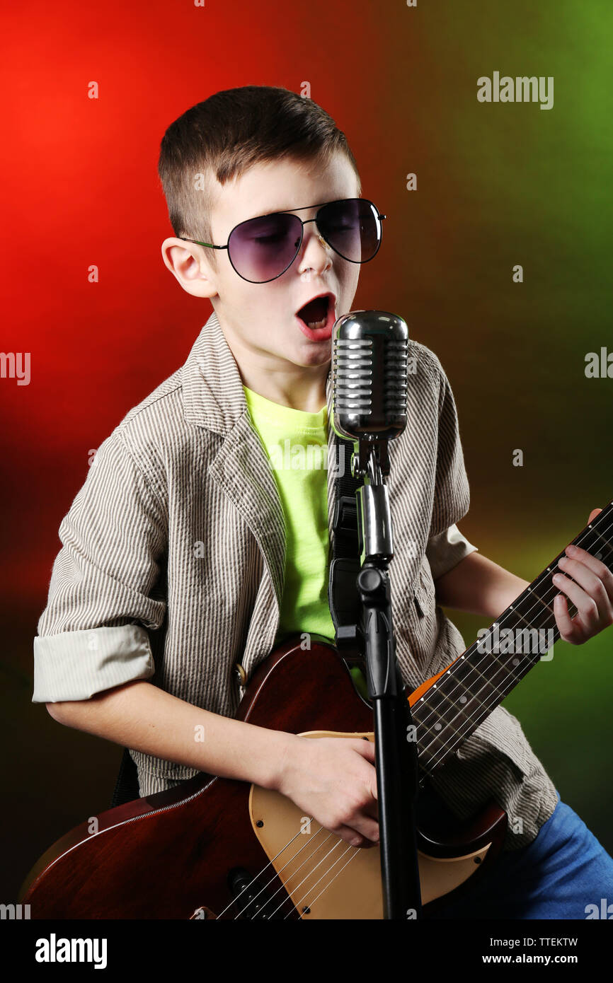 Little boy playing guitar and singing with microphone on a bright ...