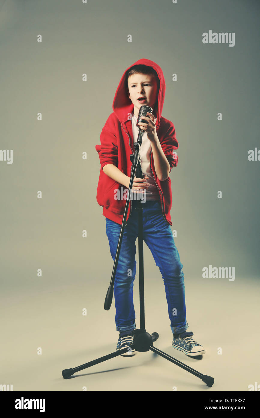 Little boy singing with microphone on a grey background Stock Photo - Alamy