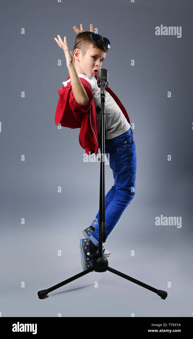 Little boy singing with microphone on a grey background Stock Photo - Alamy