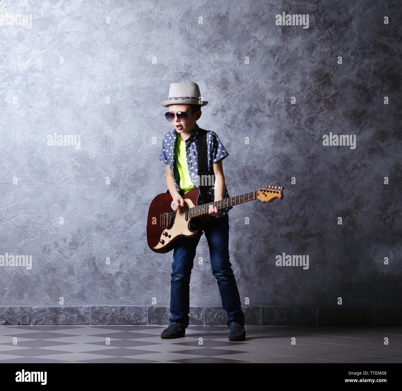 Little boy playing guitar on a grey wall background Stock Photo - Alamy