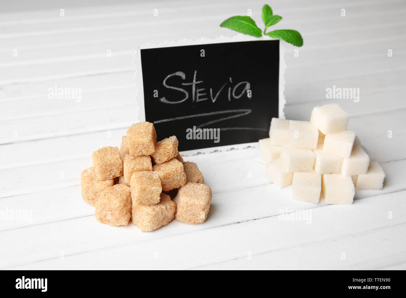 Pile of sugar cubes and stevia on white wooden background Stock Photo ...