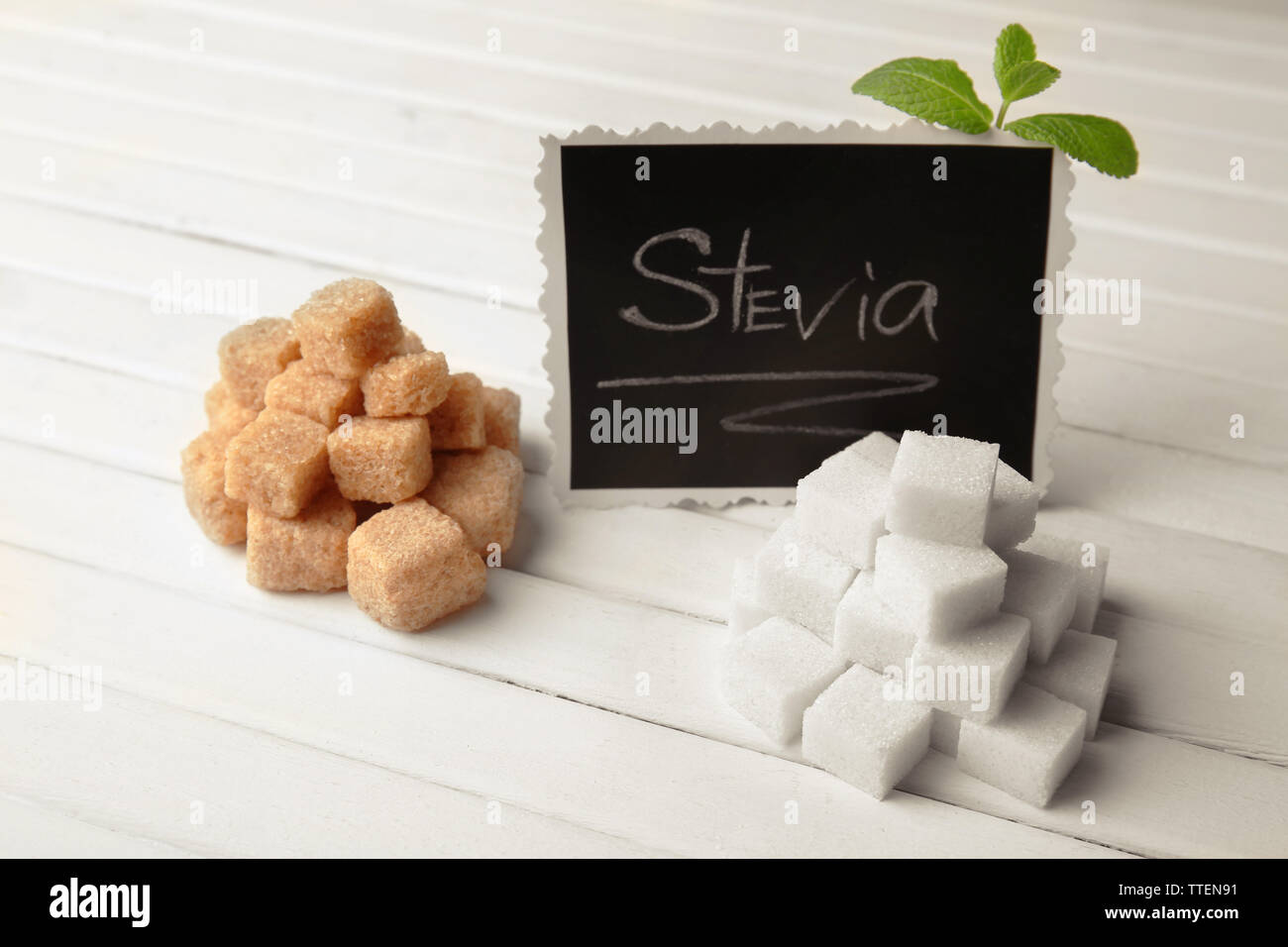Pile of sugar cubes and stevia on white wooden background Stock Photo ...