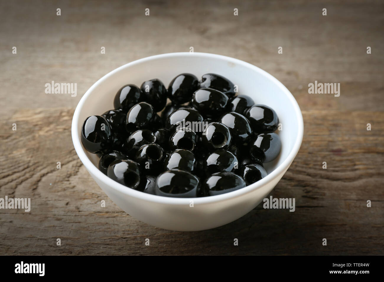 Fresh black olives in white bowl on wooden background Stock Photo - Alamy