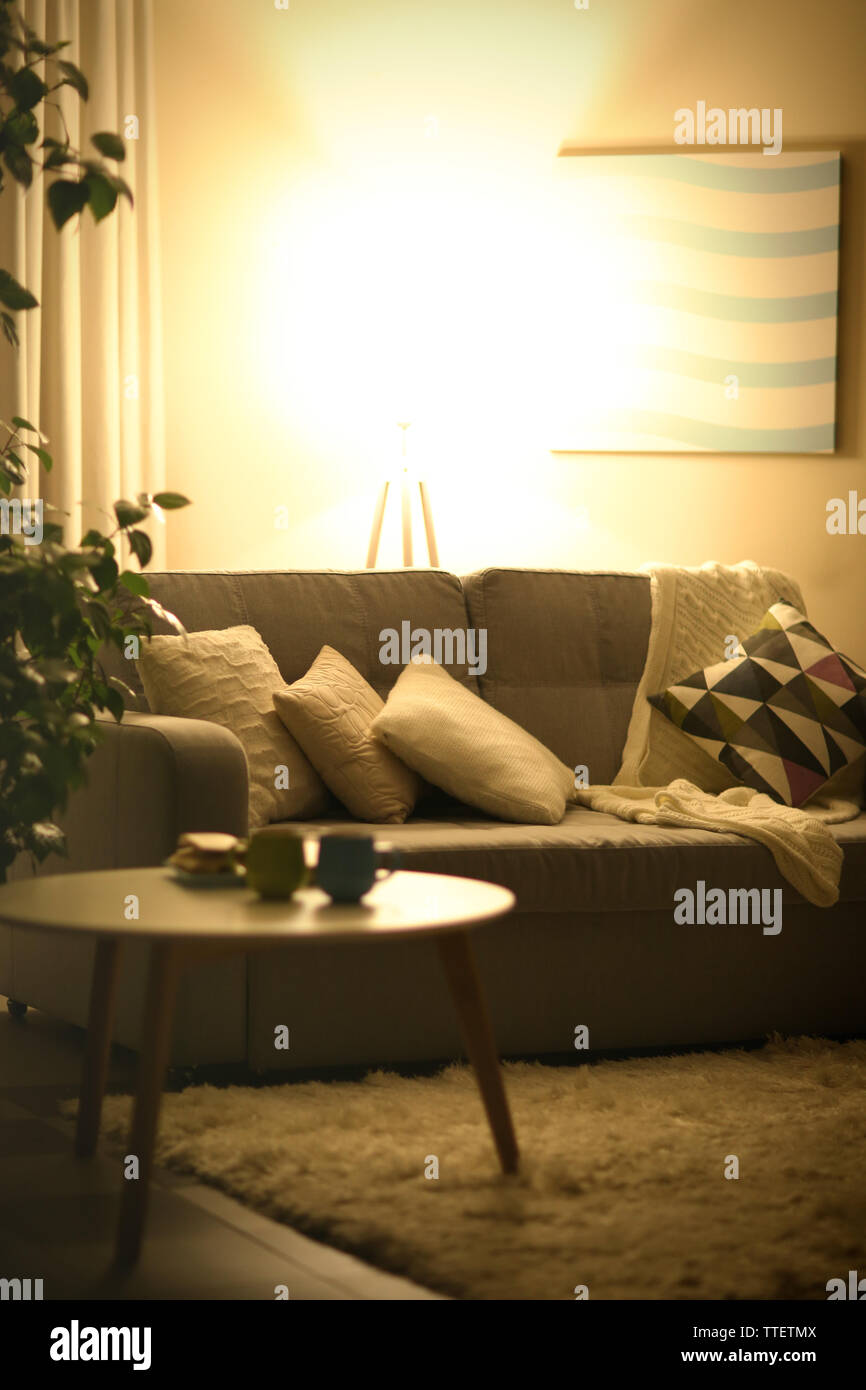 Room interior with sofa, lighted lamp and table Stock Photo - Alamy