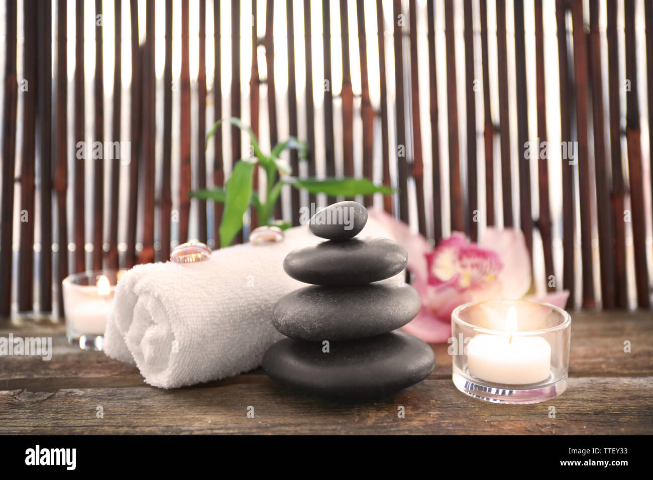 Spa stones with towel, candles, bamboo and pink orchid on wooden ...