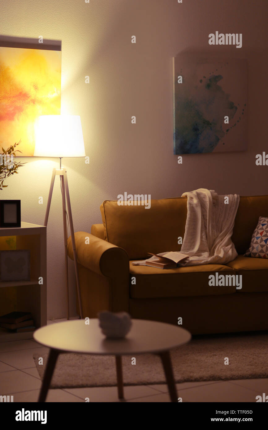 Living room interior with lighted lamp, table and green sofa Stock ...