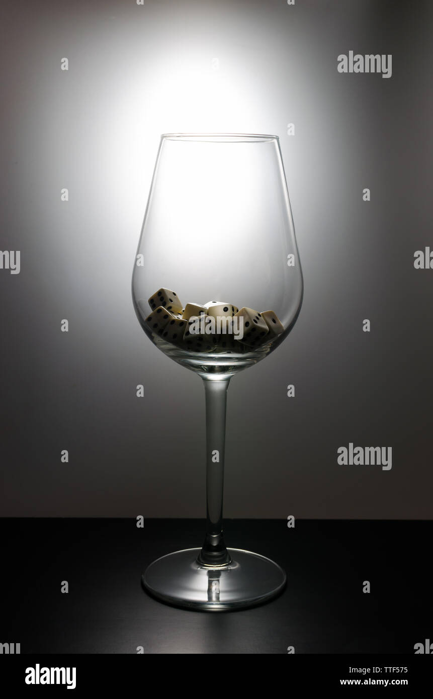Wine glass filled with dice on a grey background Stock Photo - Alamy