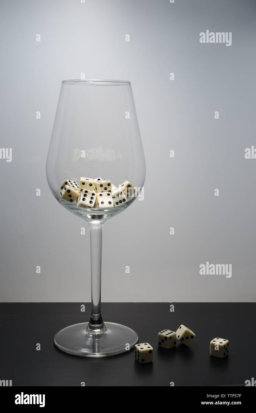 Wine glass filled with dice on a grey background Stock Photo - Alamy