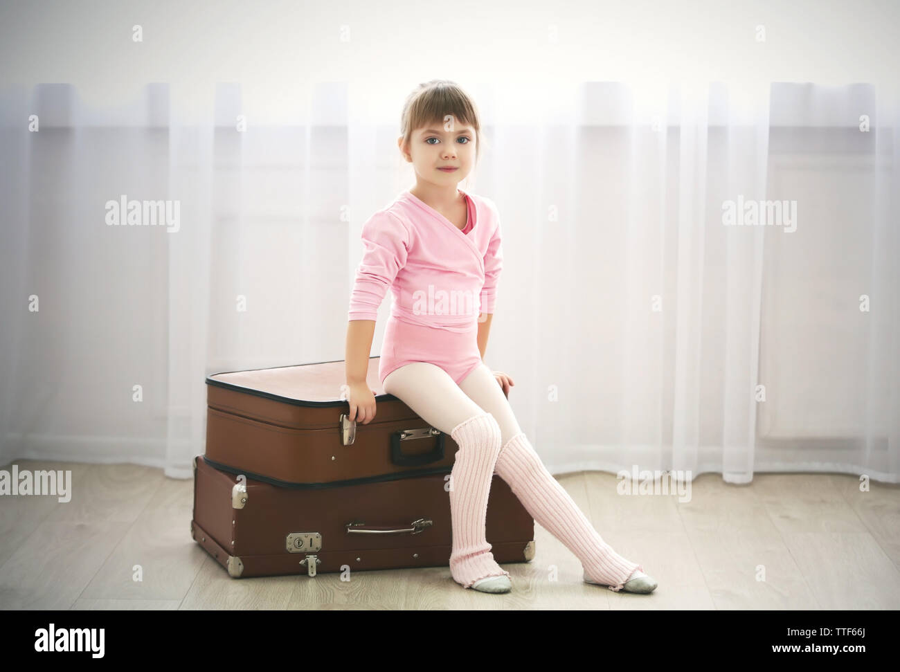 Little cute girl in pink leotard sitting on suitcases at dance studio ...