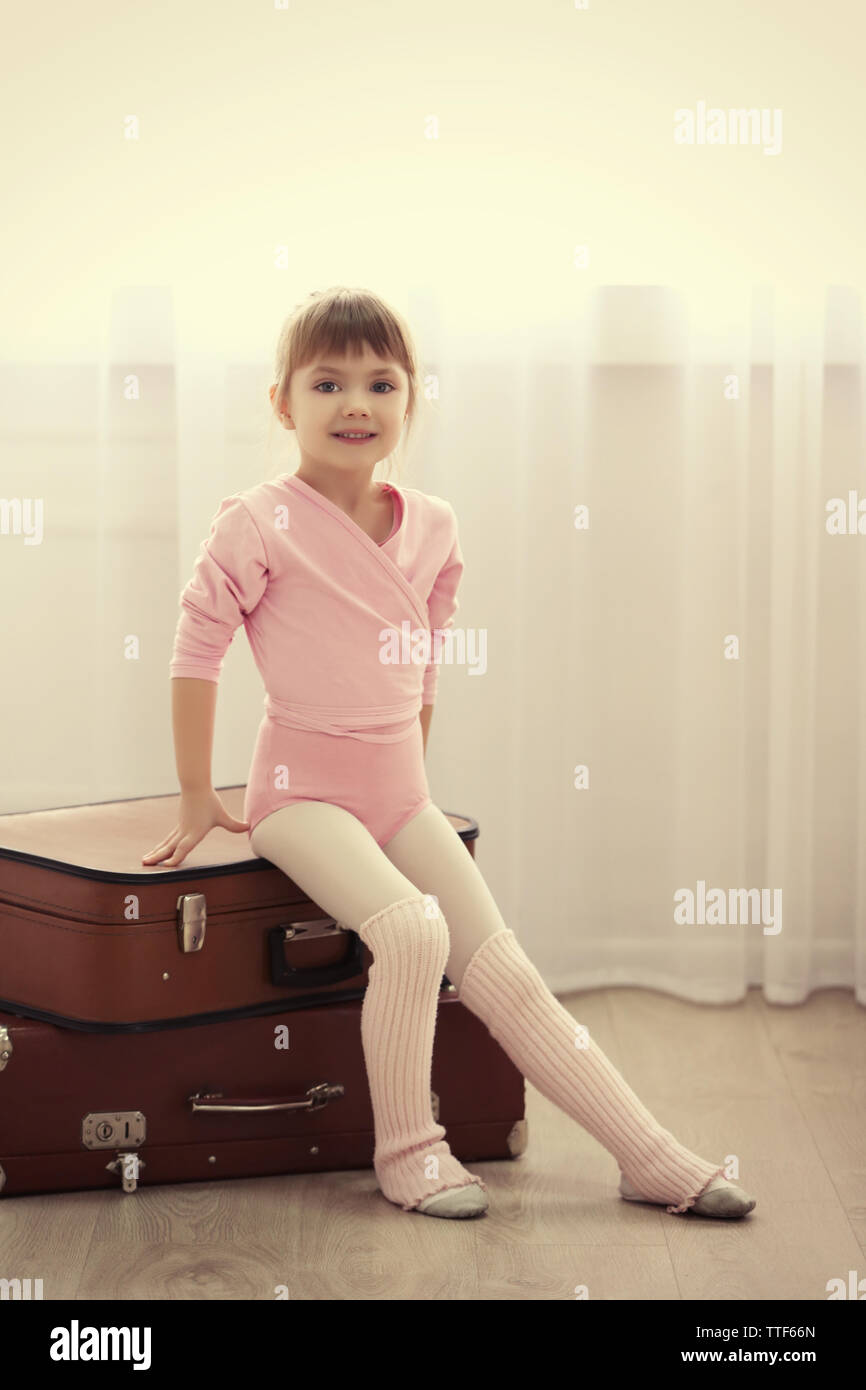Little cute girl in pink leotard sitting on suitcases at dance studio ...