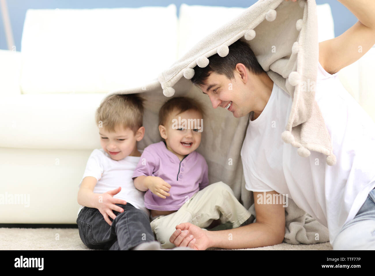 Family concept. Father with sons are playing under blanket in the room ...