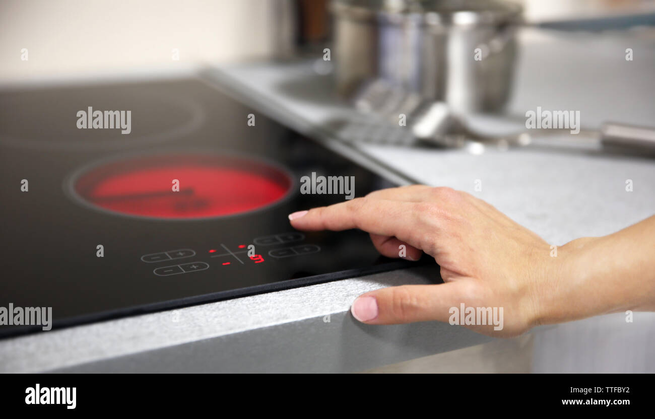 Female hand turns on electric hob closeup Stock Photo - Alamy
