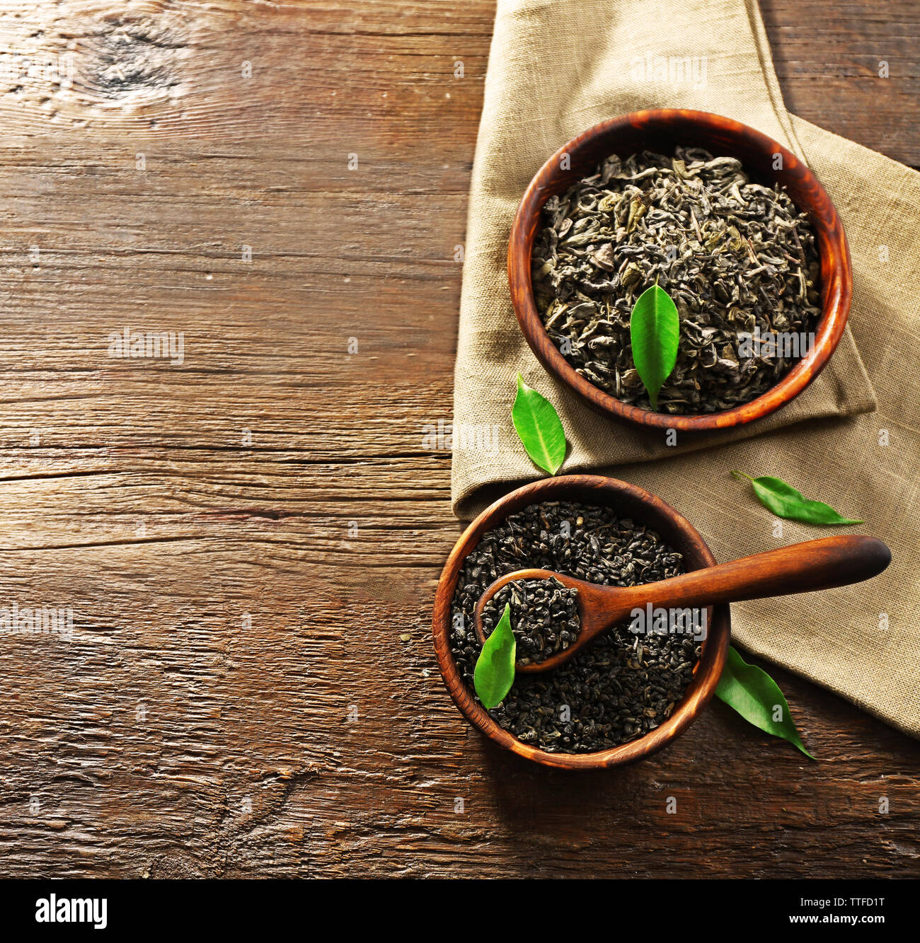 Dry tea in two bowls with green leaves on wooden table background Stock ...