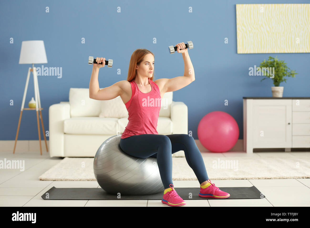 Young sportswoman doing exercises with ball and dumbbells on a mat at ...