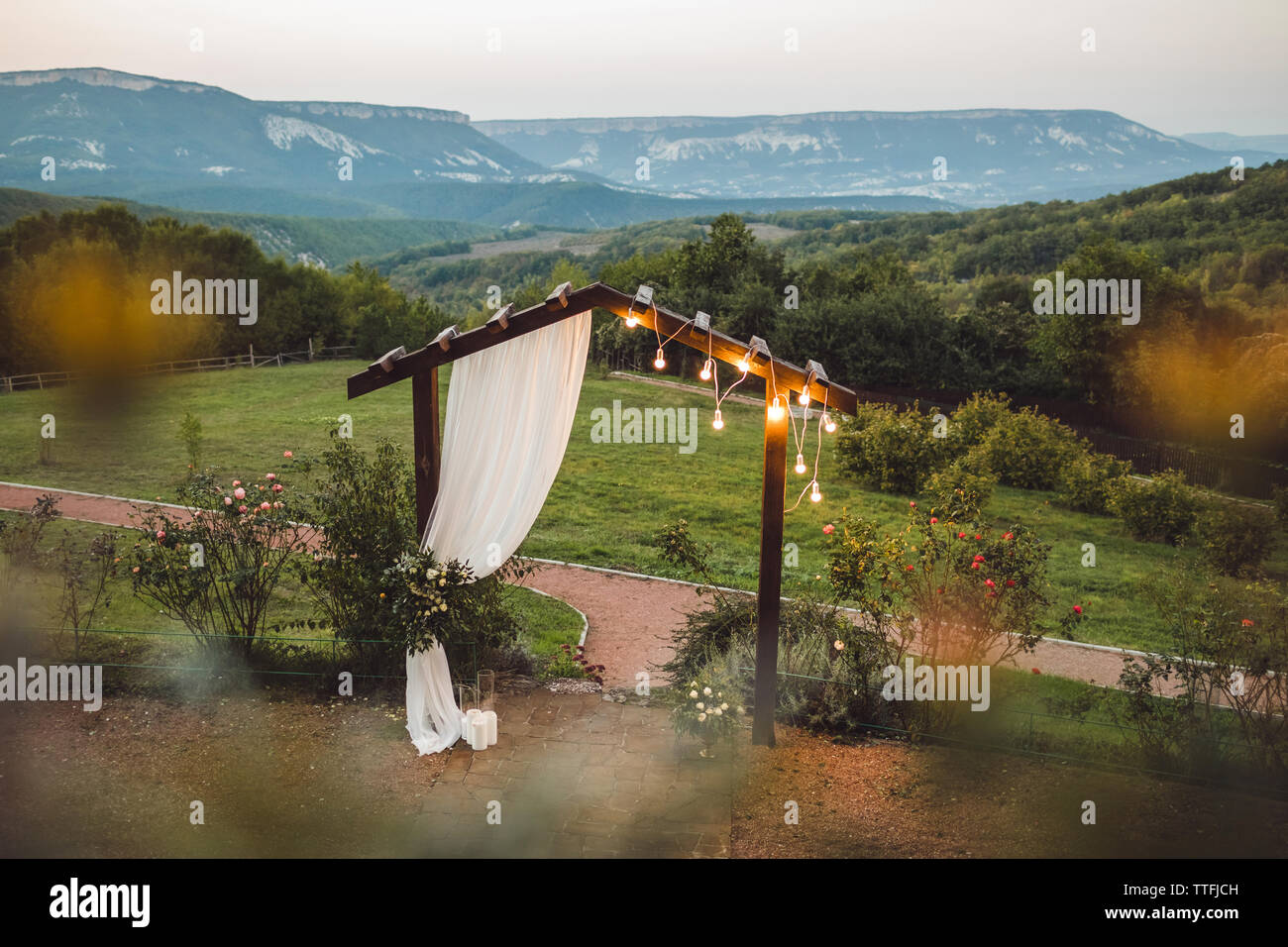 Wooden wedding arch with white cloth and light bulbs outdoors with ...