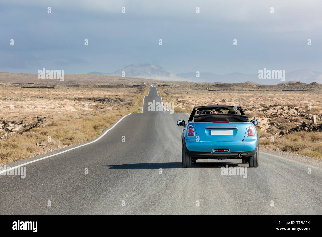 Blue cabrio car driving empty paved road in desert volcanic landscape ...
