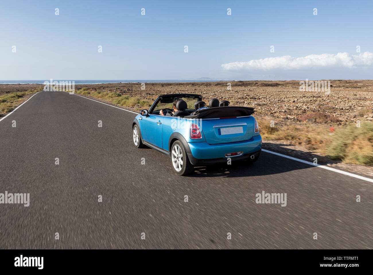 Blue cabrio car driving empty paved road in desert volcanic landscape ...