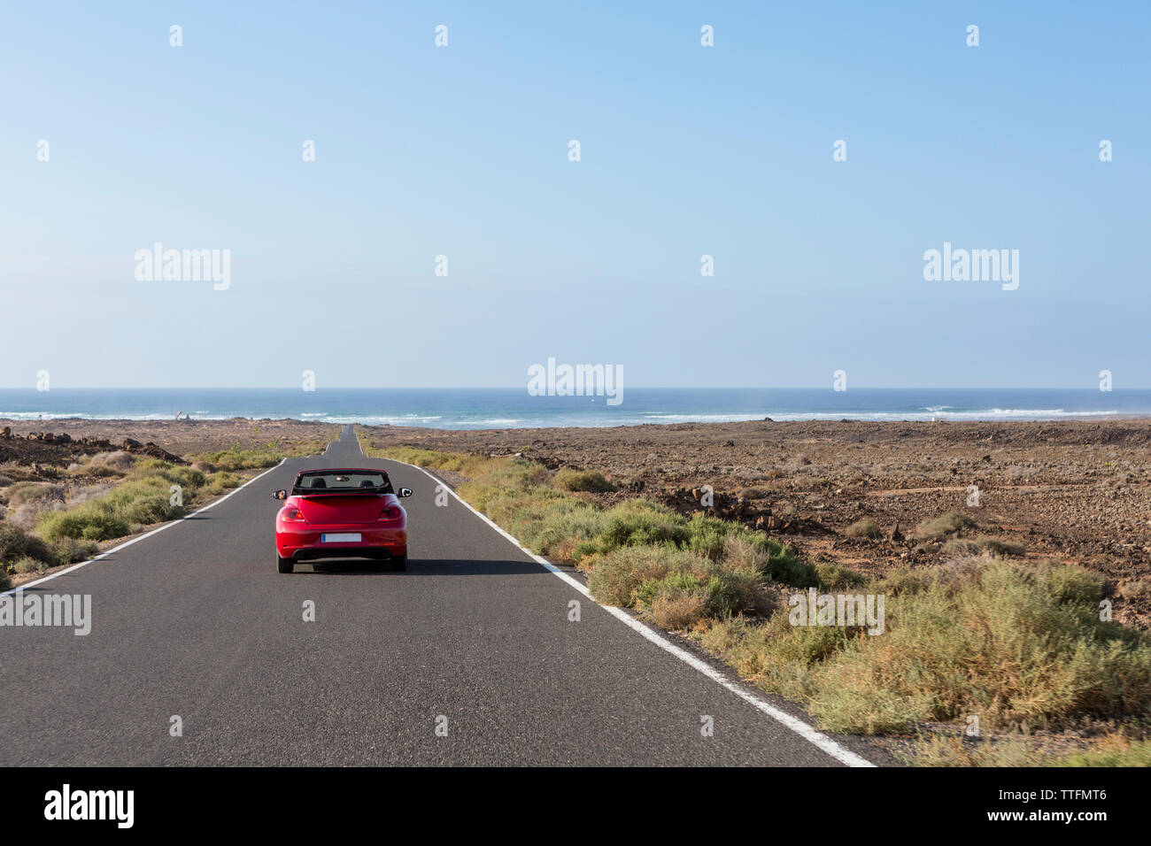 Red cabrio car driving in empty paved road towards the ocean Stock ...
