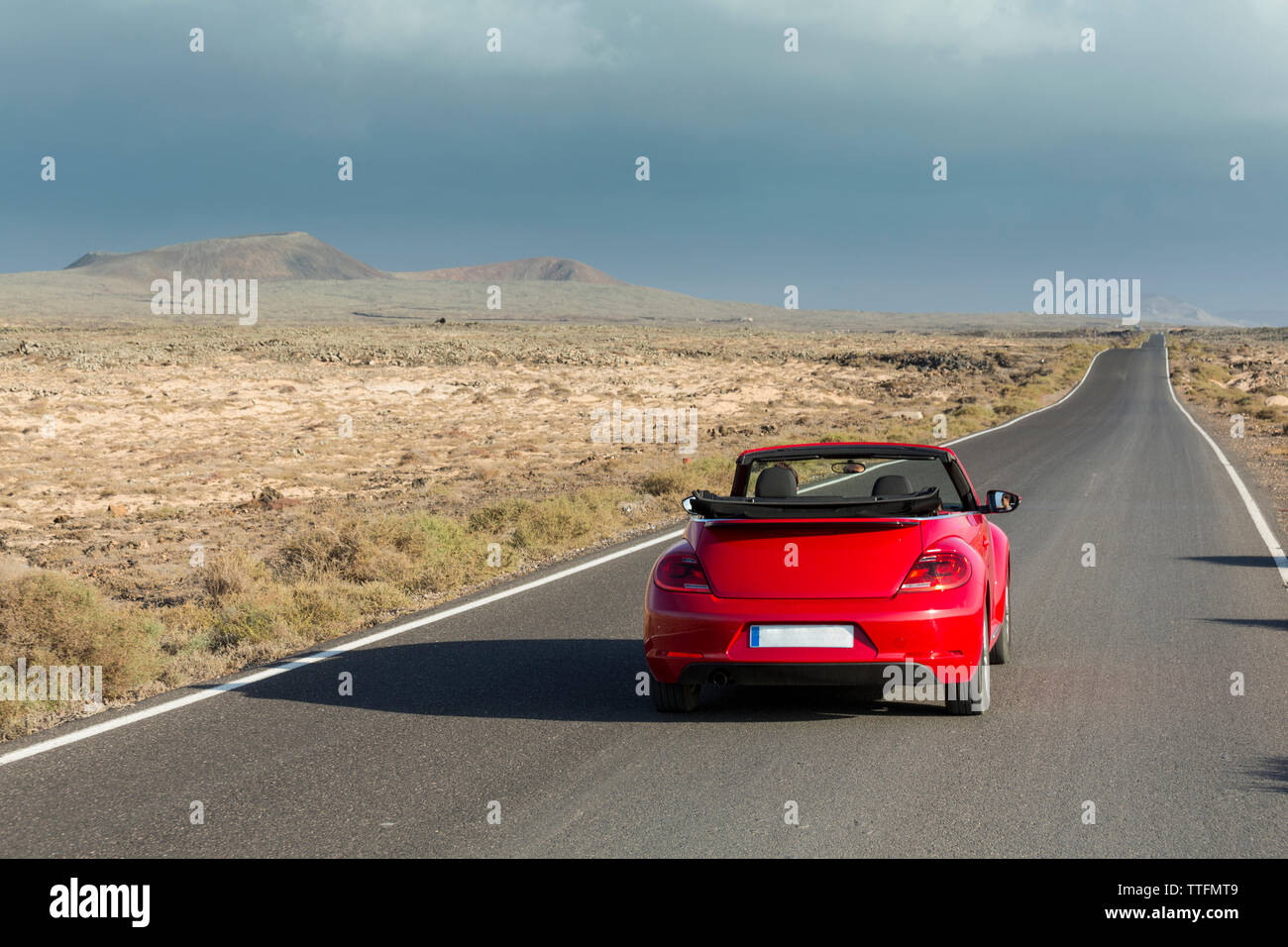 Red cabrio car driving empty paved road in desert volcanic landscape ...