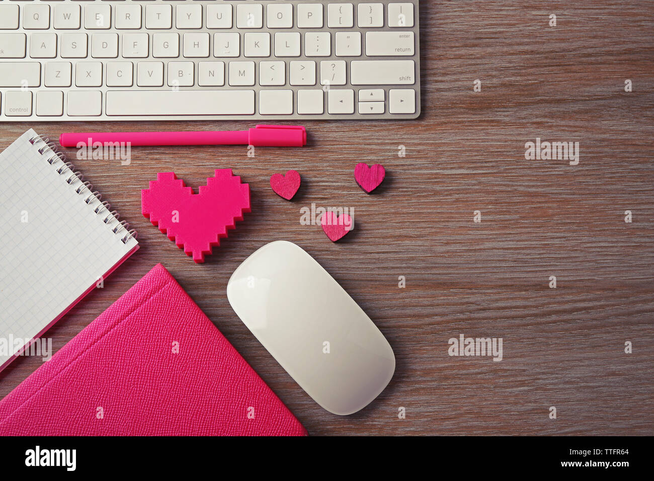 Computer peripherals with pink hearts, pen and notebooks on wooden ...