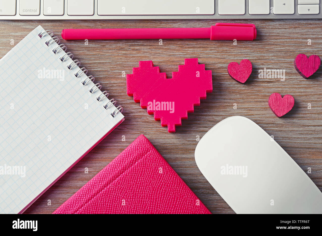 Computer peripherals with pink hearts, pen and notebooks on wooden ...