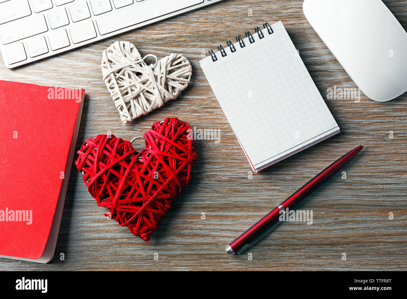 Computer peripherals with hearts, pen and notebooks on wooden table ...