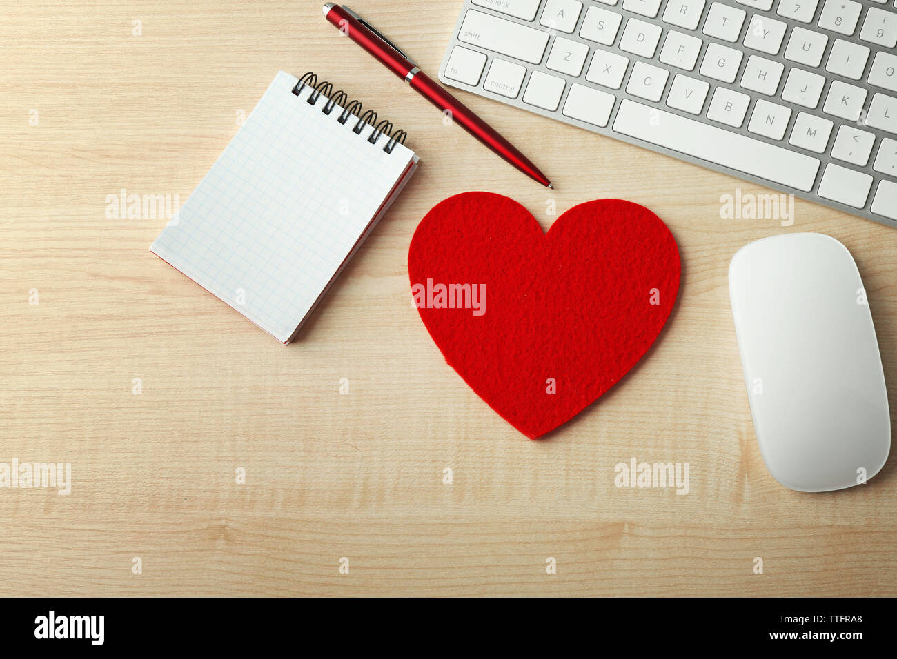 Computer peripherals with red heart, pen and notebook on light wooden ...