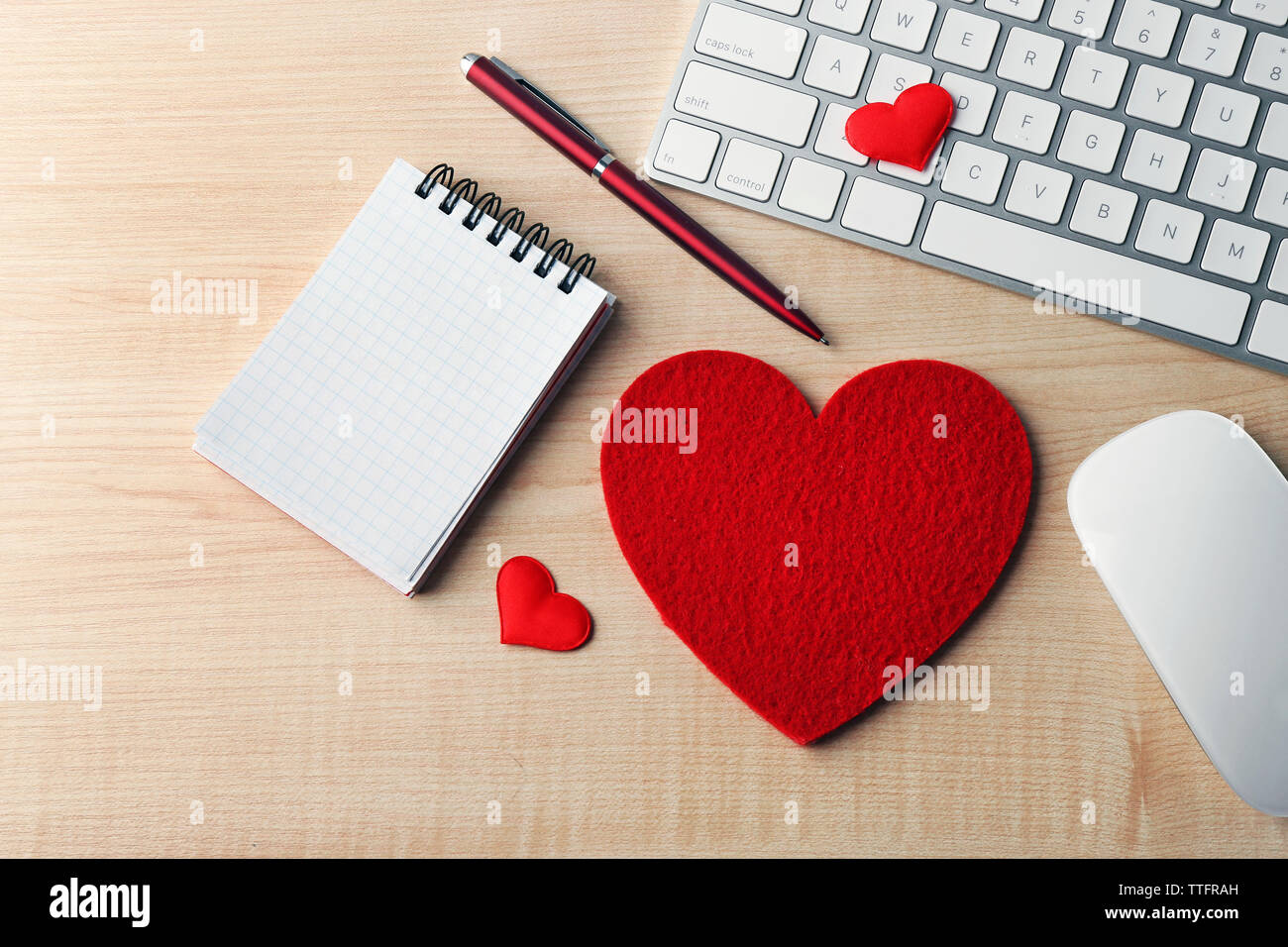 Computer peripherals with red hearts, pen and notebook on light wooden ...