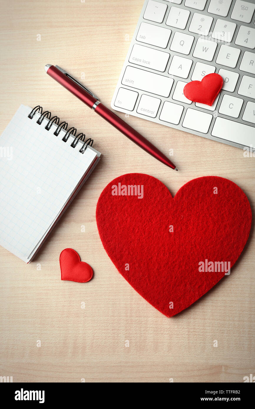 Computer peripherals with red hearts, pen and notebook on light wooden ...