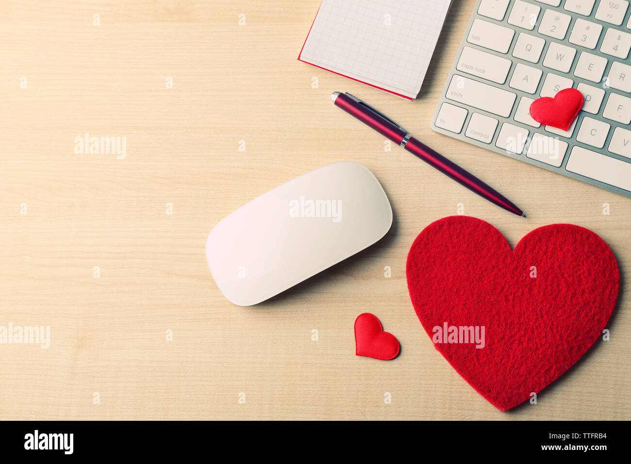 Computer peripherals with red hearts, pen and notebook on light wooden ...