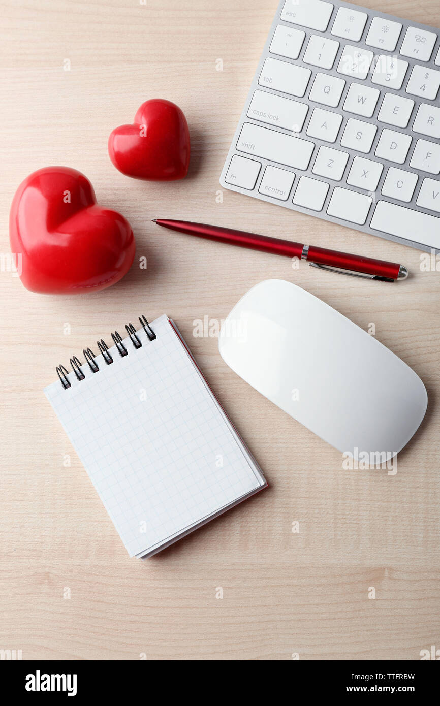 Computer peripherals with red hearts, pen and notebook on light wooden ...