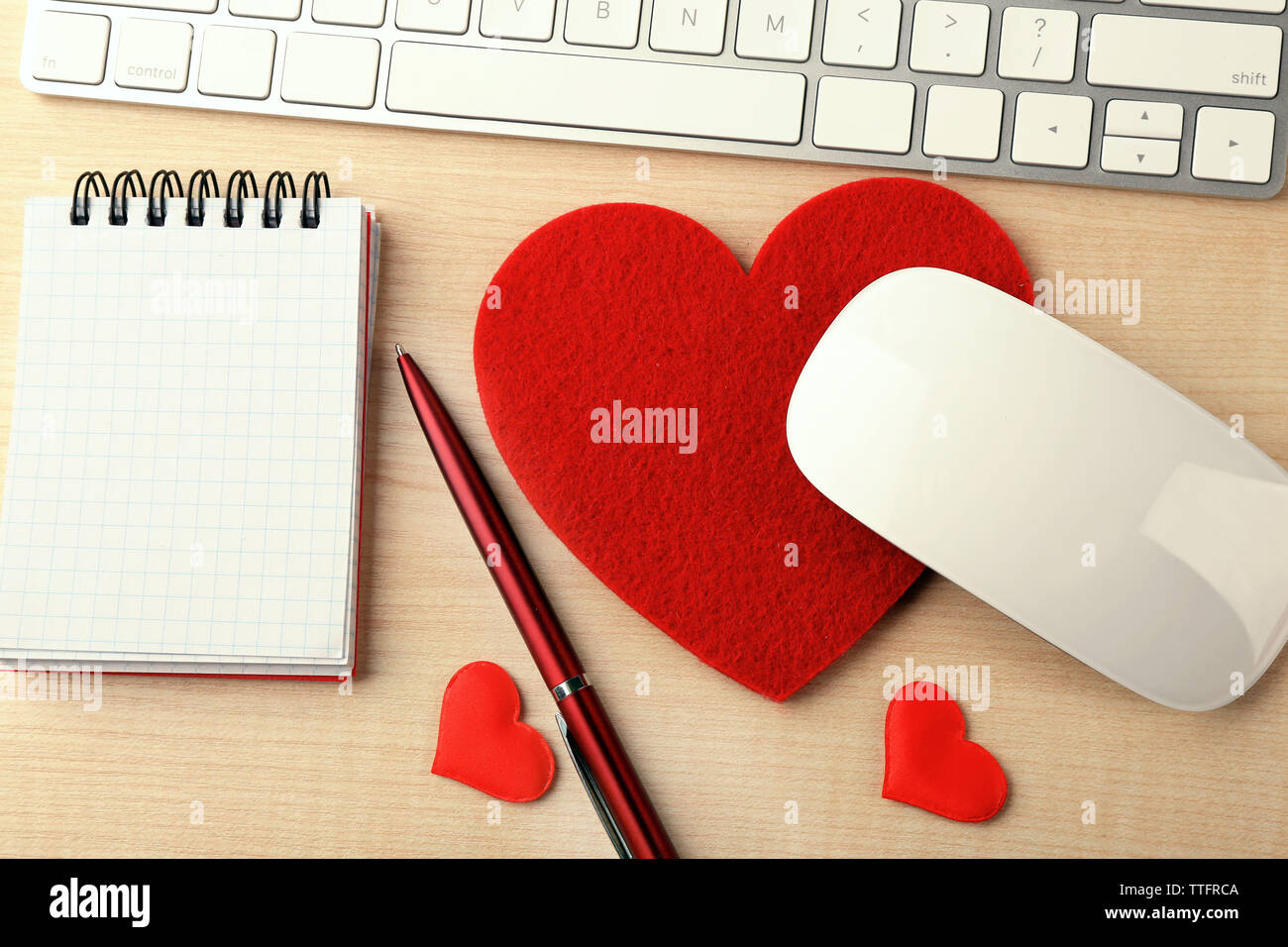 Computer peripherals with red hearts, pen and notebook on light wooden ...