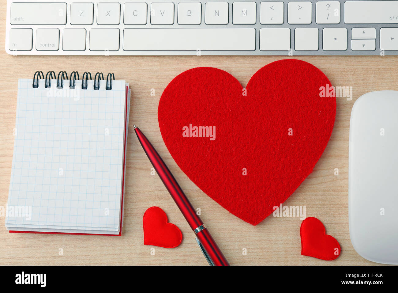Computer peripherals with red hearts, pen and notebook on light wooden ...