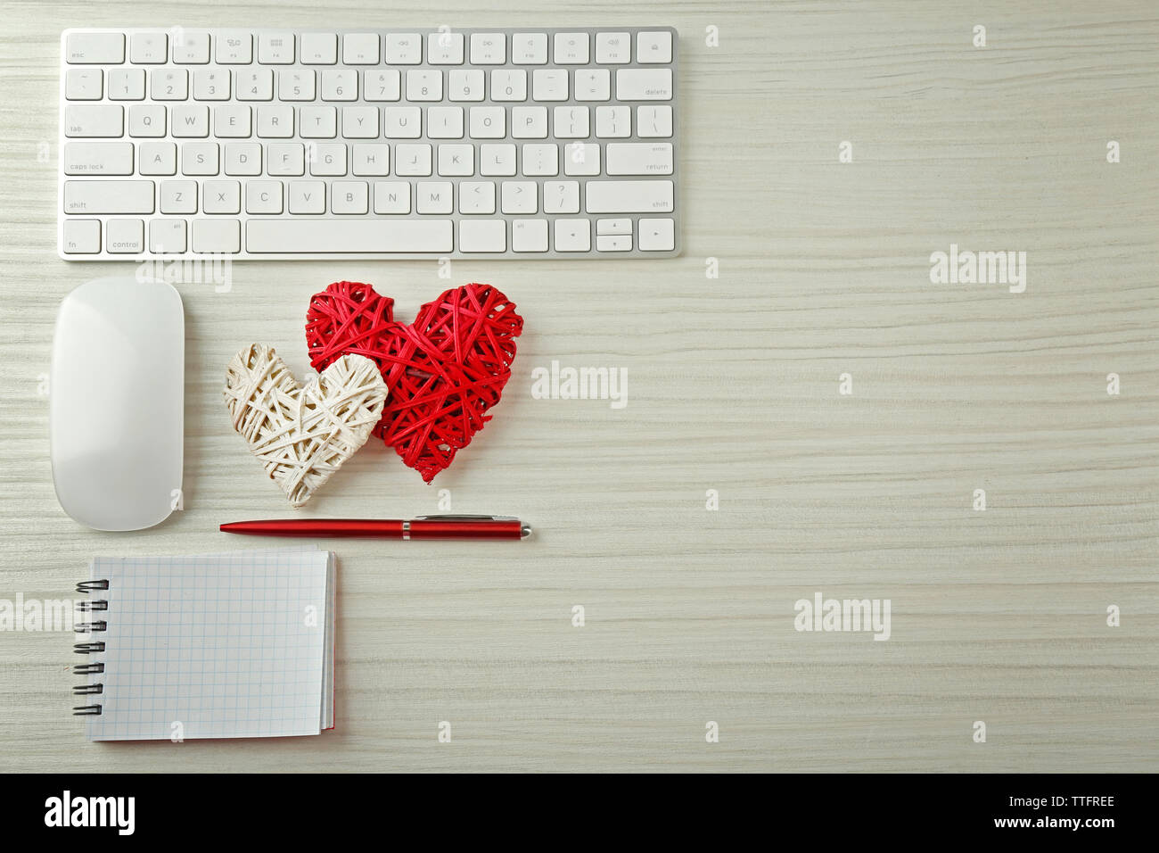 Computer peripherals with wicker hearts, pen and notebook on light ...