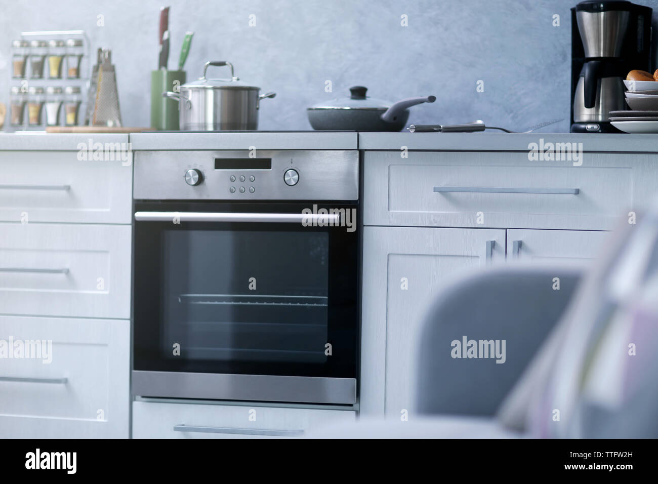 Modern kitchen interior with light furniture, electric stove and sofa ...