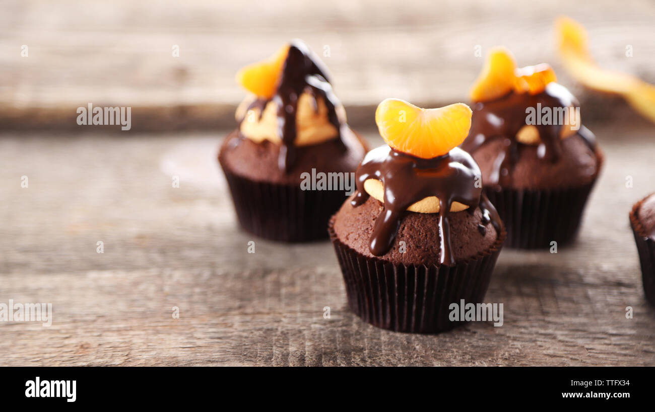 Three tasty cupcakes with slice of mandarin and chocolate on wooden ...