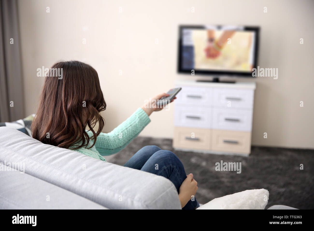 Young beautiful woman watching TV on a sofa at home Stock Photo - Alamy