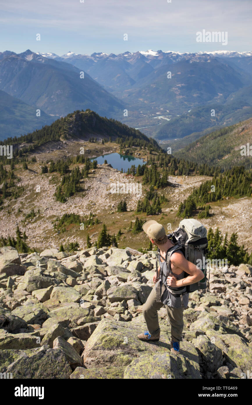 Backpacker looks down toward a tarn and alpine meadow in B.C., Canada ...