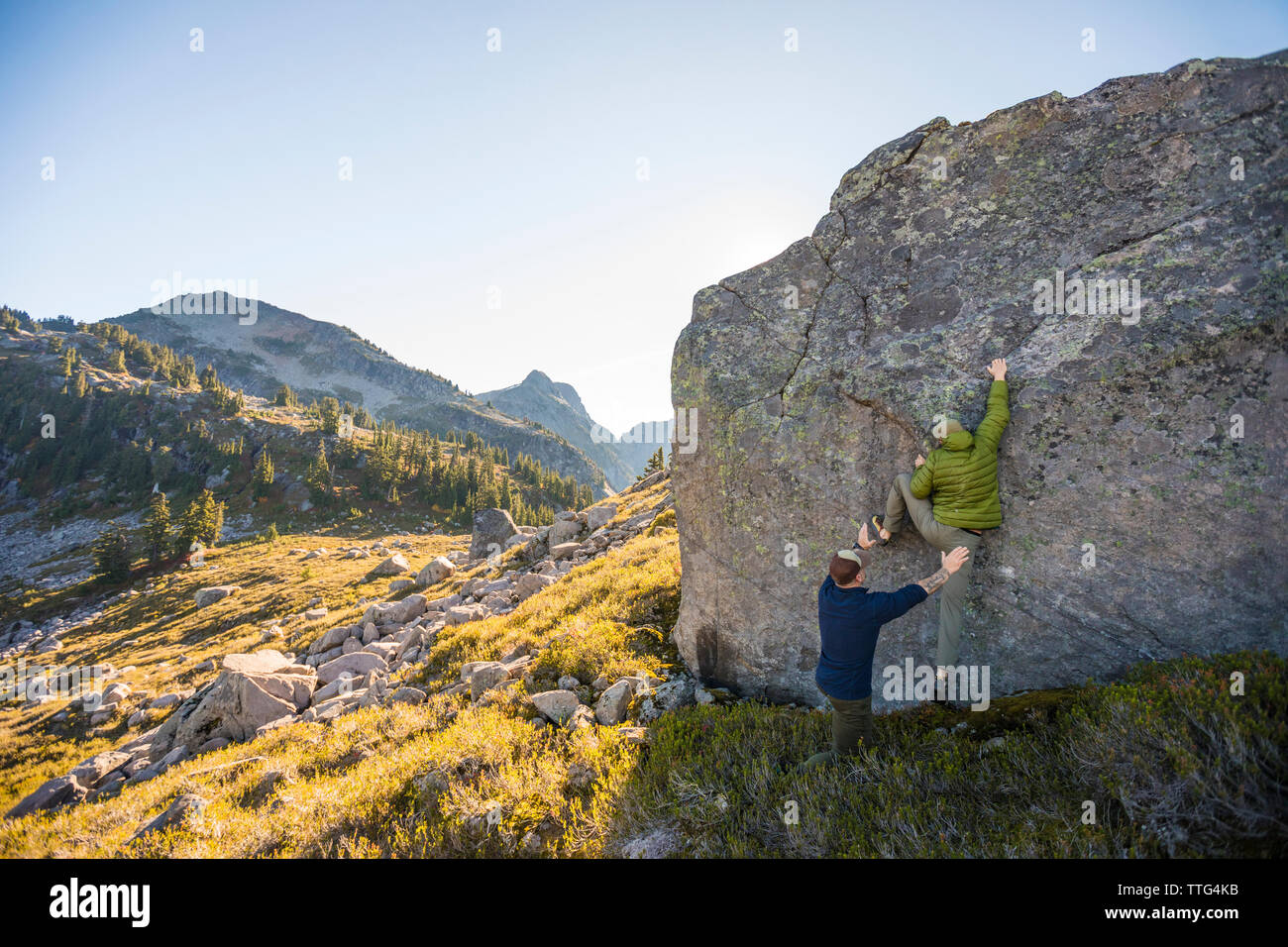 Climber bouldering on large rock with spotter below Stock Photo - Alamy