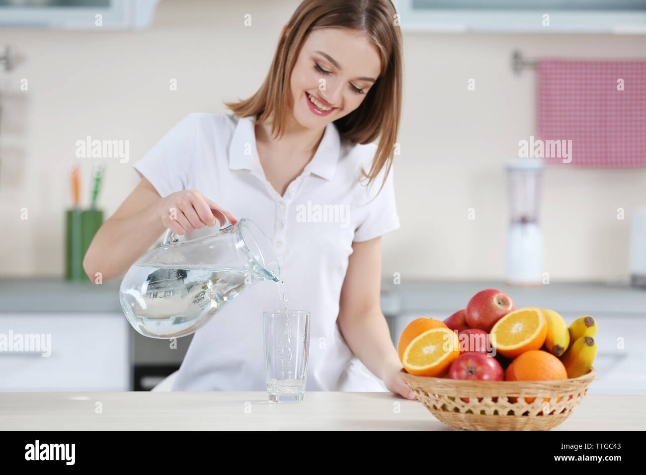 Young woman pouring water from jug into glass in the kitchen Stock Photo - Alamy