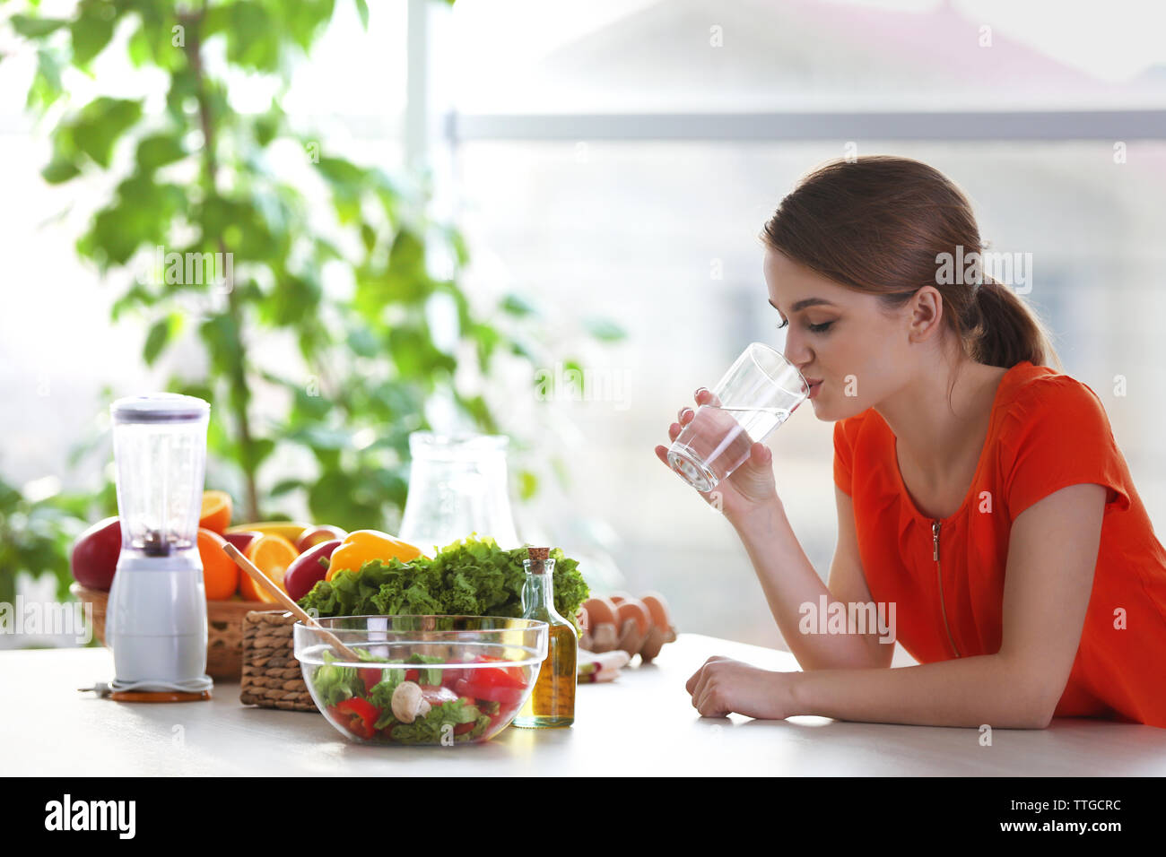 Young woman drinking water near table with fruits and vegetables in the kitchen Stock Photo - Alamy