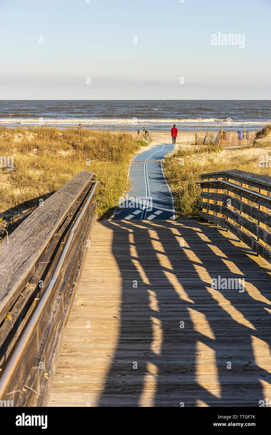 Ocean views draw a young woman across a boardwalk and onto sandy beach ...