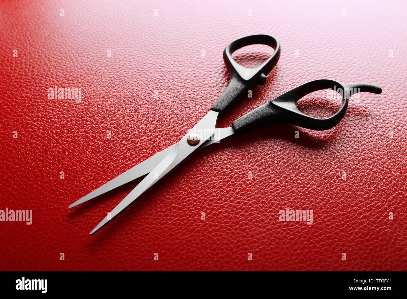 Professional scissors with black handles lying on red leather surface ...