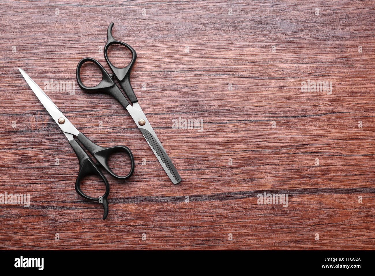 Two professional metal scissors with black handles lying on the wooden ...