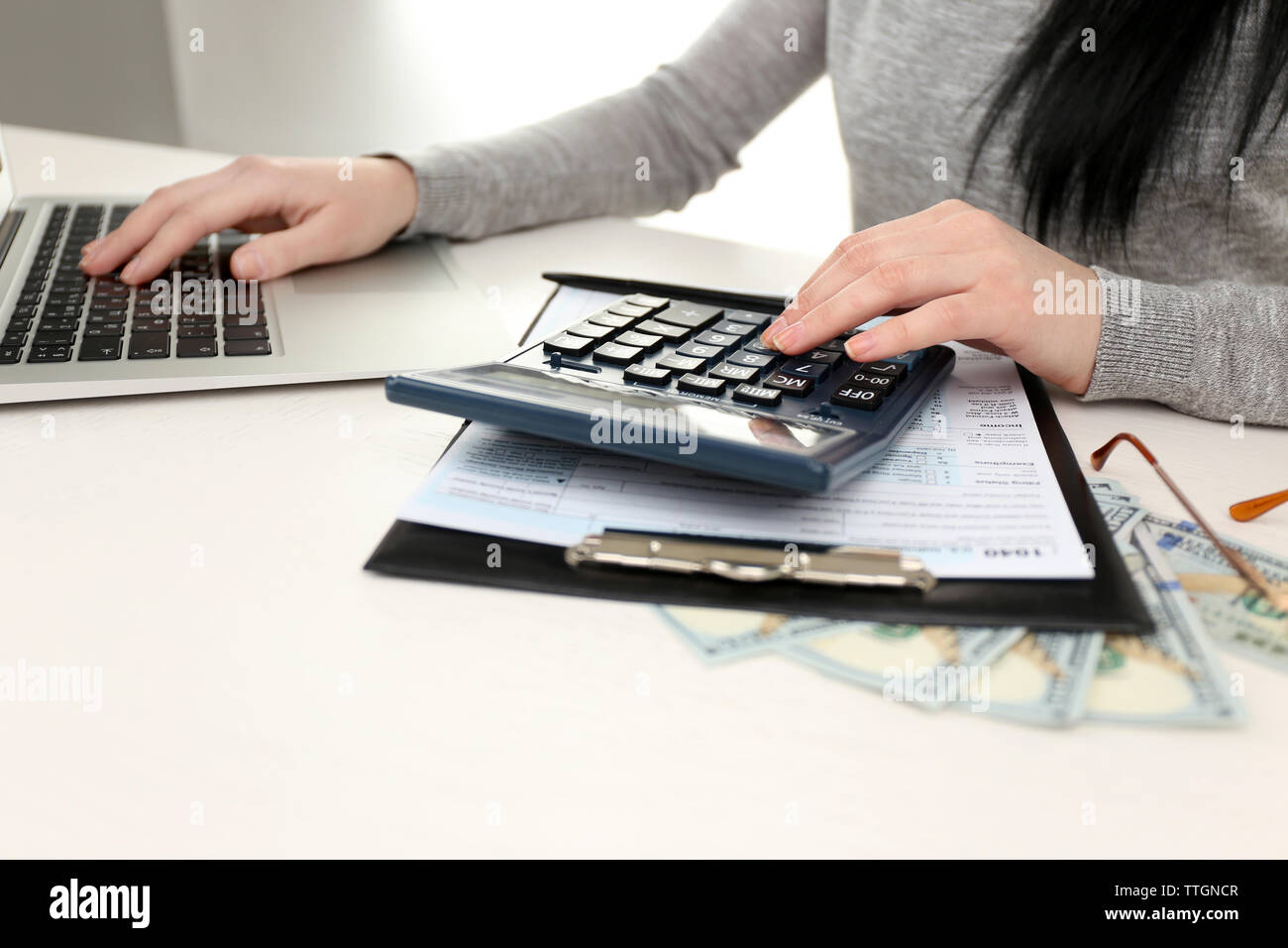 Dark-haired woman calculating while using computer on the white wooden ...
