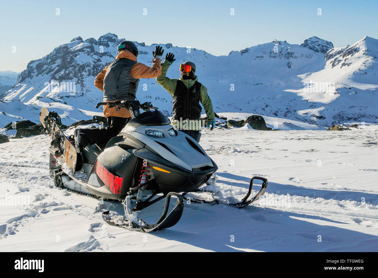 Two friends hi five after a fun day of snowmobile access skiing Stock ...